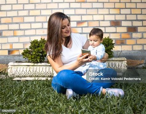 어머니는 휴대 전화로 무릎에 작은 아들과 함께 풀밭에 앉아 있습니다 모성 베이비 케어 엄마와 아이들 사이의 상호 작용 및 기술에 대한 언급 2명에 대한 스톡 사진 및 기타