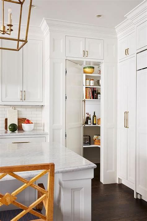 A White Hidden Pantry Door Fixed Beneath White Kitchen Cabinets Is