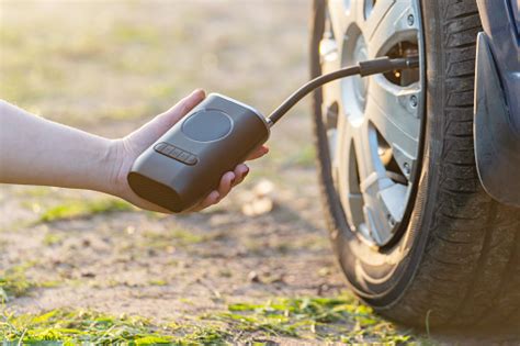 한 여성의 손이 자동차 타이어에 공기를 주입하기 위한 무선 휴대용 공기 펌프를 들고 있다 계기판 측정기에 대한 스톡 사진 및 기타 이미지 계기판 측정기 공기 주입