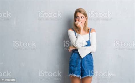 강조 하 고 손톱을 물어 뜯고 입에 손을 긴장을 찾고 그런 지 회색 벽에 서 있는 아름 다운 젊은 여자 불안 문제입니다 감정에 대한 스톡 사진 및 기타 이미지 Istock