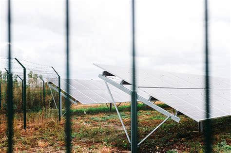 太陽能電池板或光伏農場背後金屬鏈圍欄在綠地與戲劇性的多雲天空在德國北部 照片檔及更多 可持續資源 照片 可持續資源 大自然 天空