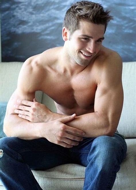 A Shirtless Man Sitting On Top Of A Couch Next To A Blue Wall And Smiling