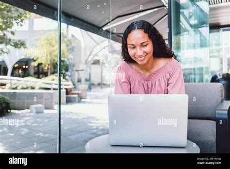 Happy Young Latin Student Woman Using A Laptop And Sitting Outside A