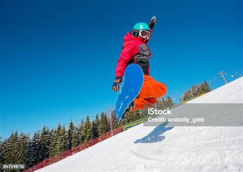 낮은 각도의 Snowboarder 아름 다운 화창한 겨울 날에 산에 언덕에 타고 있는 동안 공중에 점프 샷 숲 푸른 하늘 및