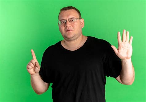 Hombre con sobrepeso en gafas con camiseta negra mostrando y señalando