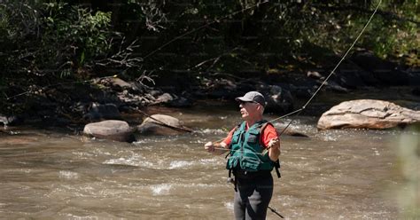Un Hombre Parado En Un Río Mientras Sostiene Una Caña De Pescar Foto
