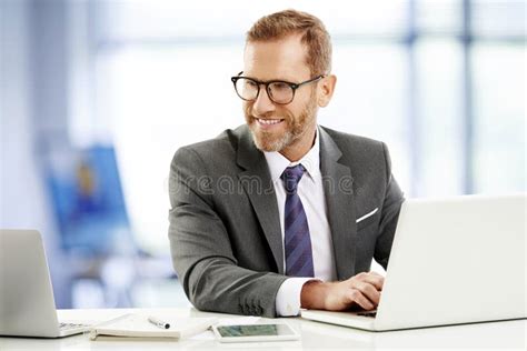 Confident Mid Aged Businessman Using Laptops For Work At The Office