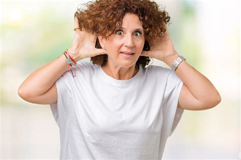 아름 다운 중간 어른 고위 여자 손으로 청각 소문 또는 험담을 듣고 귀에 웃 고 고립 된 배경 위에 흰색 T셔츠를 입고 난청 개념입니다 T 셔츠에 대한 스톡 사진 및 기타