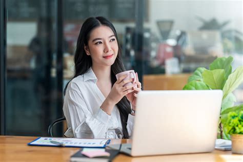 사무실에서 일하는 커피 잔과 노트북을 들고 미소 짓는 아름다운 젊은 아시아 사업가 사무실에 대한 스톡 사진 및 기타 이미지