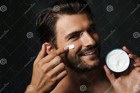 Hombre Joven Semidesnudo Sonriendo Mientras Aplica Crema De Cara Imagen