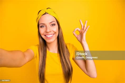 Okey 기호를 보여주는 셀카를 만드는 예쁜 아가씨의 클로즈업 사진은 캐주얼 T 셔츠를 입고 고립 된 노란색 배경 개성 개념에
