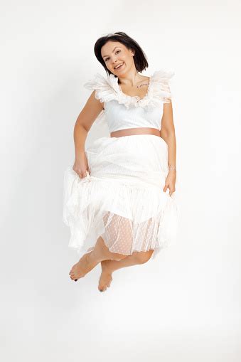 맨발의 행복한 성인 갈색 머리 여자는 흰색 배경 복사 공간에 고립 된 바람이 잘 통하는 낭만적 인 흰색 드레스를 즐겁게 뛰어 넘습니다 홀리데이 룩 이벤트 축하 우아한 여성