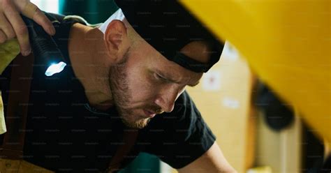 노란색 자동차의 열린 후드 위로 손전등을 구부리고 결함을 확인하고 차고에서 모터 부품을 고정하는 진지한 자동차 정비사 사진 Unsplash의 사진술 이미지