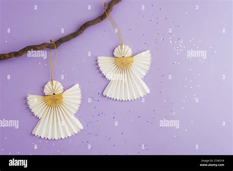 Two Christmas Paper Angels Hanging On The Tree Branch On Purple