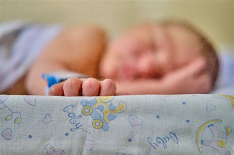 손에 출산 병원 팔찌를 팔에 안고 있는 신생아가 침대에서 자고 있습니다 투명 유리 뒤에 클리닉 침대에서 새로 태어난 아이 1