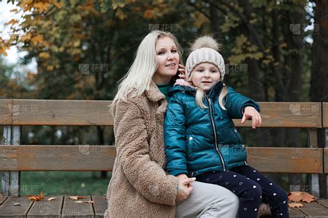 幸福家庭，母女在秋城公园。他们摆姿势，微笑，玩耍，玩得很开心。亮黄色的树木。