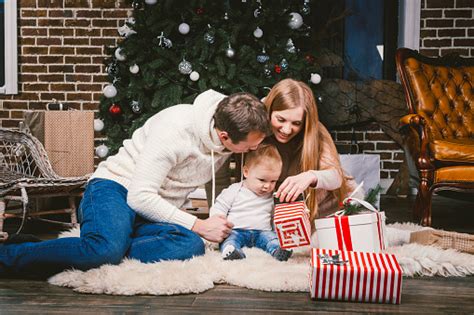 가족 기념 크리스마스 저녁입니다 침 엽 수 아래 가족 3 백인 사람들이 나무 카펫 모직의 층에 크리스마스 트리 아이 선물 세련 된 옷을 입고 젊은 부모와 함께 상자를 보유