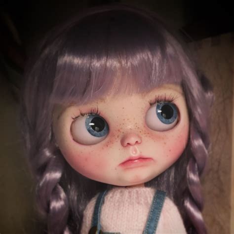 A Close Up Of A Doll With Blue Eyes And Purple Hair Wearing Overalls