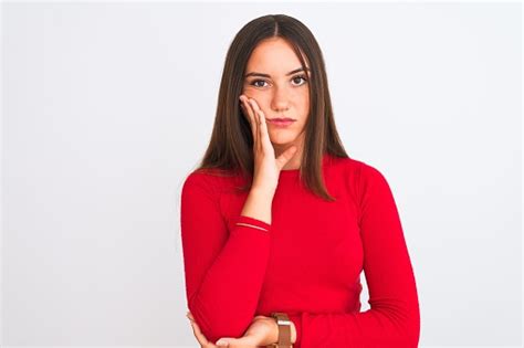 빨간 캐주얼 티셔츠를 입고 있는 어린 소녀는 고립된 흰색 배경 위에 서서 피곤하고 교차 된 팔로 우울증 문제로 지루해보입니다 갈색 머리에 대한 스톡 사진 및 기타 이미지