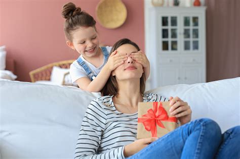 어린 소녀는 흥분 된 부모에게 생일 선물을 미소 어린 아이는 행복한 어머니와 닫힌 어머니의 눈에 선물 상자를 제공합니다 축하합니다 가족에 대한 스톡 사진 및 기타 이미지