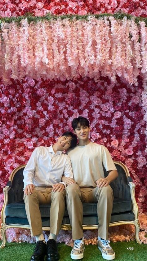 Two People Are Sitting On A Couch In Front Of A Flower Wall With Pink