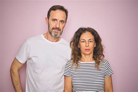 아름다운 중년 부부는 얼굴에 심각한 표정으로 고립 된 분홍색 배경 위에 함께 서 있습니다 카메라를 보는 간단하고 자연스러운 2명에 대한 스톡 사진 및 기타 이미지 Istock