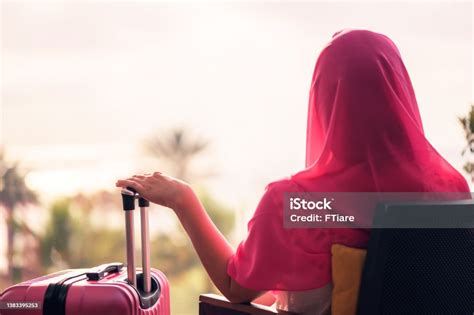 무슬림의 실루엣 붉은 머리 스카프를 입은 아랍 여성 테라스에서 가방을 들고 안락의자에 앉아 일몰 야자수 바다 해변을 바라보는