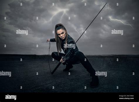 A Female In Black Ninja Assassin Costume Holding A Sword Lighting In