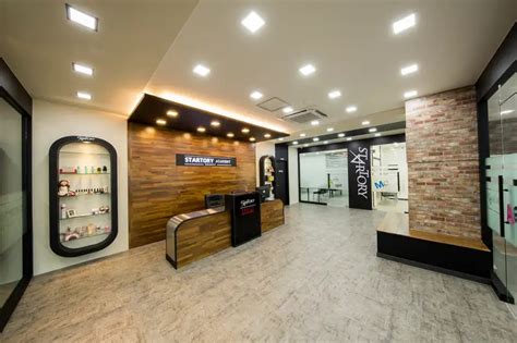 뷰티 아카데미 화이트톤 바탕에 짙은 우드톤의 포인트 벽과 데스크와 블랙 포인트 선반과 붙박이 소파가 있는 로비 대기 공간 사진