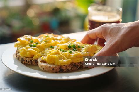 아침에 건강한 아침 식사를 즐기면서 스크램블 에그를 얹은 구운 빵 한 조각을 들고 있는 여성의 손이 잘린 이미지 달걀에 대한