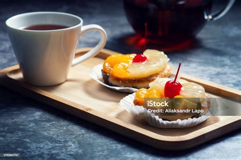 차 한 잔과 체리를 얹은 파인애플 거꾸로 된 케이크 두 개를 배경에 찻주전자가 있는 나무 쟁반에 놓습니다 0명에 대한 스톡 사진 및 기타 이미지 Istock