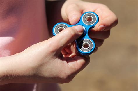 회색 배경 스트레스와 이완 Fidgets 안티 불안 구제 장난감 인기 있는 피 젯 회전자 장난감을 들고 거리 여성 손에 손에 파란 금속 회전자를 재생 하는 여자 강철에 대한