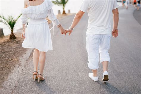 하얀 옷을 입은 연인 몇 명이 바다 근처 도로를 따라 걷고 있으며 한 여성이 부드럽게 남자의 손을 잡고 있습니다 2명에 대한