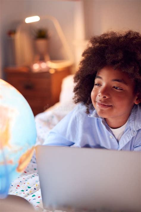 Boy In Bedroom At Night Lying On Bed Using With Laptop With Illuminated