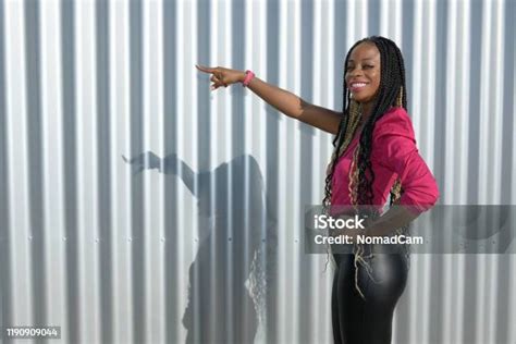 긴 검은 색과 금발 머리띠가 왼쪽을 가리키고 배경에 금속 울타리가있는 카메라를 바라보는 동안 미소를 짓는 아프로 스타일의 흑인