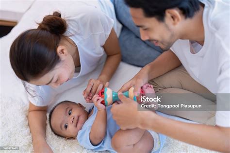 엄마와 아버지는 웃는 즐거운 자랑스러운 놀림 키스 뺨과 발 팔을 잡고 침대에서 새로 태어난 아시아 유아 아기를 잡고 부모에 대한 스톡 사진 및 기타 이미지 Istock