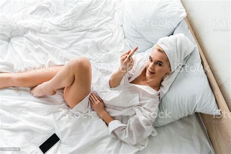 스마트 폰 근처에 흰 침대에 누워 머리에 수건을 가진 보석의 맨발 여자의 평면도 및 표시 가운데 손가락 개인 장식품에 대한 스톡