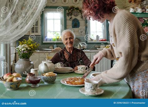 Feliz Anciana Sentada En La Mesa Servida Y Mirando A Una Chica Cortando