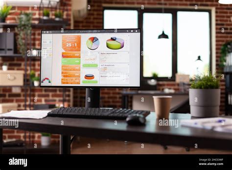 Computer With Business Charts On Desk In Empty Workplace Monitor With