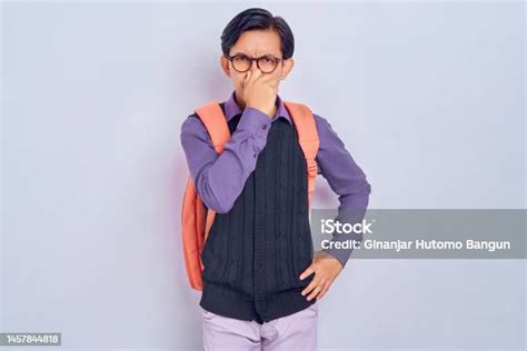 배낭을 메고 캐주얼한 옷을 입은 젊은 아시아 학생 남자가 카메라를 바라보며 회색 배경에 고립된 손으로 코를 가리고 있다 고등학교