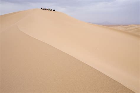 이란 야즈드의 거대한 오렌지 사막 모래 언덕에 앉아 있는 사람들의 배경을 배경으로 한 모래 언덕 꼭대기의 트레일 건조한에 대한