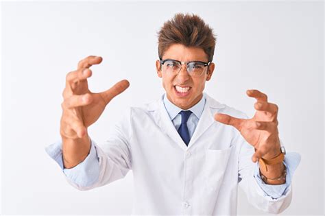 고립된 흰색 배경 위에 안경과 코트를 입은 젊은 잘생긴 Sciencist 남자분노로 좌절 외치고 손은 목을 매고 미친 소리를