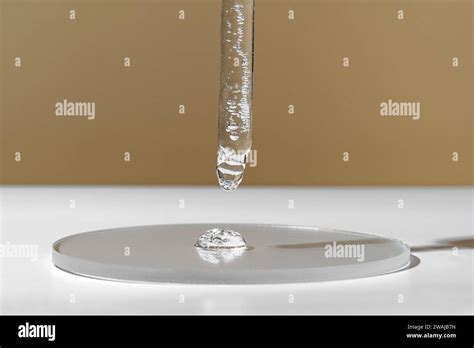 A Precise Dropper Releases A Single Clear Liquid Drop Onto A Glass Surface Against A Neutral