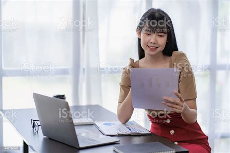 노트북 컴퓨터로 일하는 아시아 사업가 계산 분석 젊은 여성 재정 고문 통계 보고서 준비 문서 연구 사무실에서 재무 차트 확인
