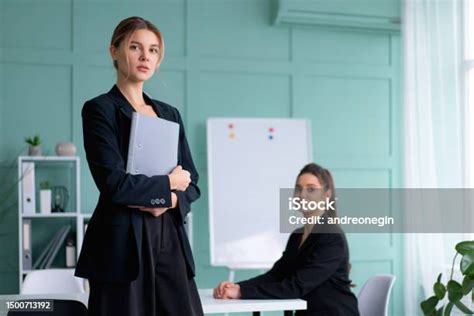 사무실에서 검은 양복을 입은 두 명의 청녀 지도자가 한 여성이 사진 폴더에 앉아 있는 다른 여성이 카메라를 바라보고 있다