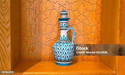 파란색과 흰색의 기하학적 패턴으로 장식된 우아한 주전자는 조각된 나무 틈새에 놓여 있어 장인 정신과 전통적인 미학을 보여줍니다 0명에 대한 스톡 사진 및 기타 이미지