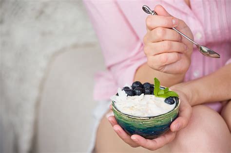 여자의의 손을 잡고 컵 블루베리와 코코넛 신선한 민트 유기농 요구르트와 함께 여자의 손에서 수 제 바닐라 요구르트입니다 아침 식사 간식 건강 한 식습관과 라이프 스타일 개념