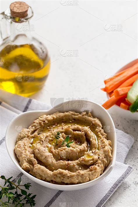 一个碗里的鹰嘴豆泥酱芝麻橄榄油黄瓜和胡萝卜放在一个明亮的背景上