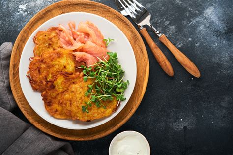 감자 팬케이크 오래된 검은 테이블 배경에 소박한 접시에 크림 파 마이크로 그린 붉은 연어와 소스와 함께 집에서 만든 감자 팬케이크 또는 라켓 튀김 소박한 스타일 맨 위