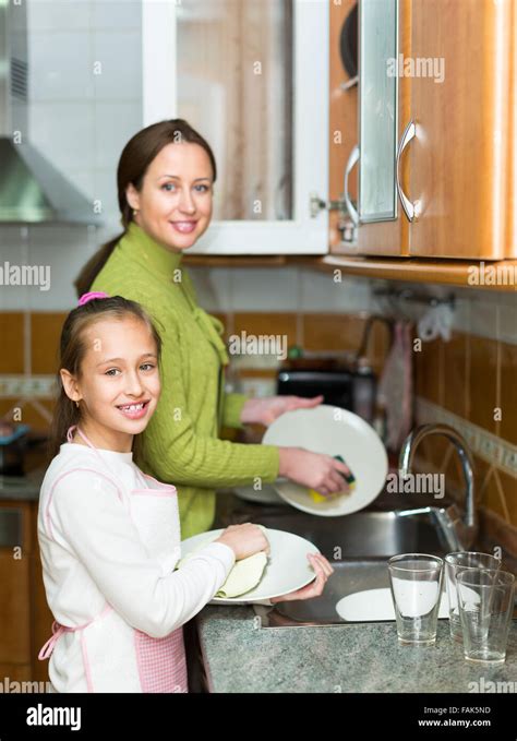 Little Smiling Daughter Helping Mother Washing Dishes In The Kitchen